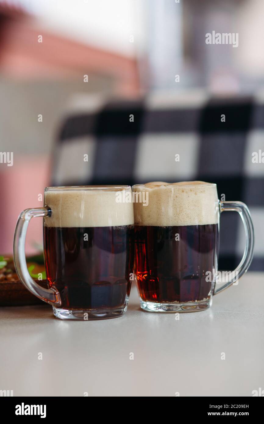Two big glass cups full of foamy cold beer standing on pub's table ...