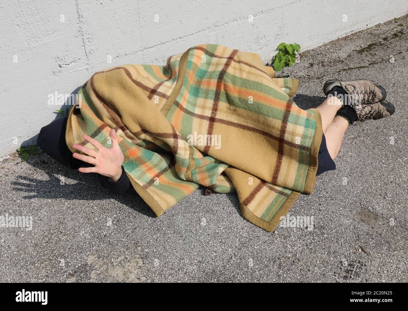 young homeless man under an old blanket and his hand raised to protect ...