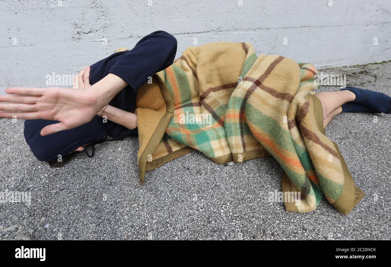 annoyed homeless young man raises his hand from under a filthy blanket ...