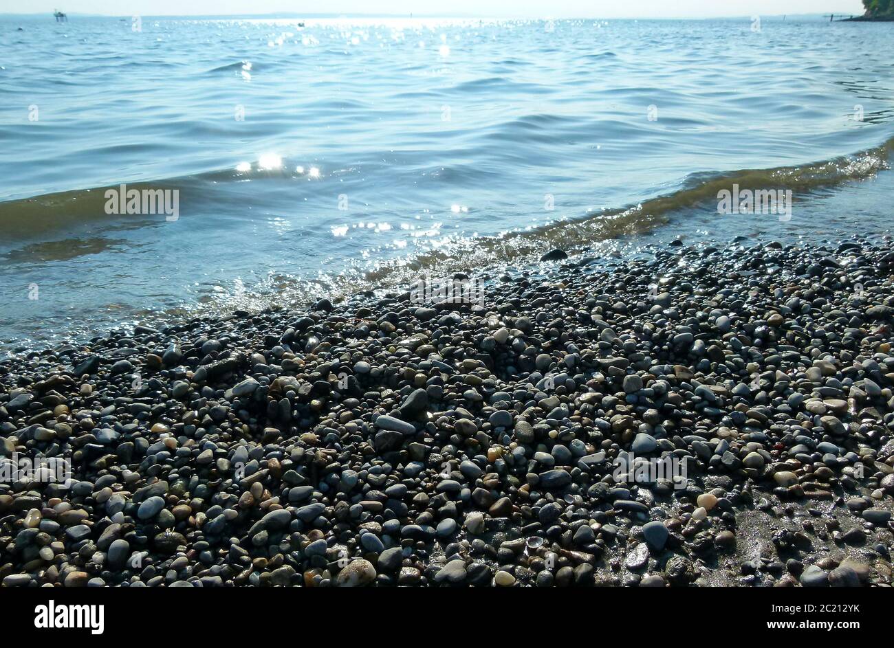 Lakeshore with gravel beach and sun reflexes hi-res stock photography ...