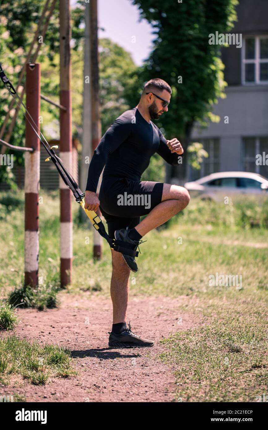 Young man exercising with suspension trainer sling in City Park under ...