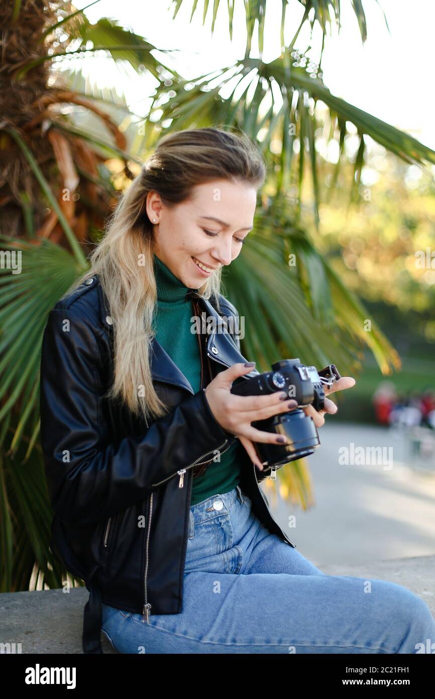 Blonde girl sitting with camera outside near palm leaves Stock Photo ...