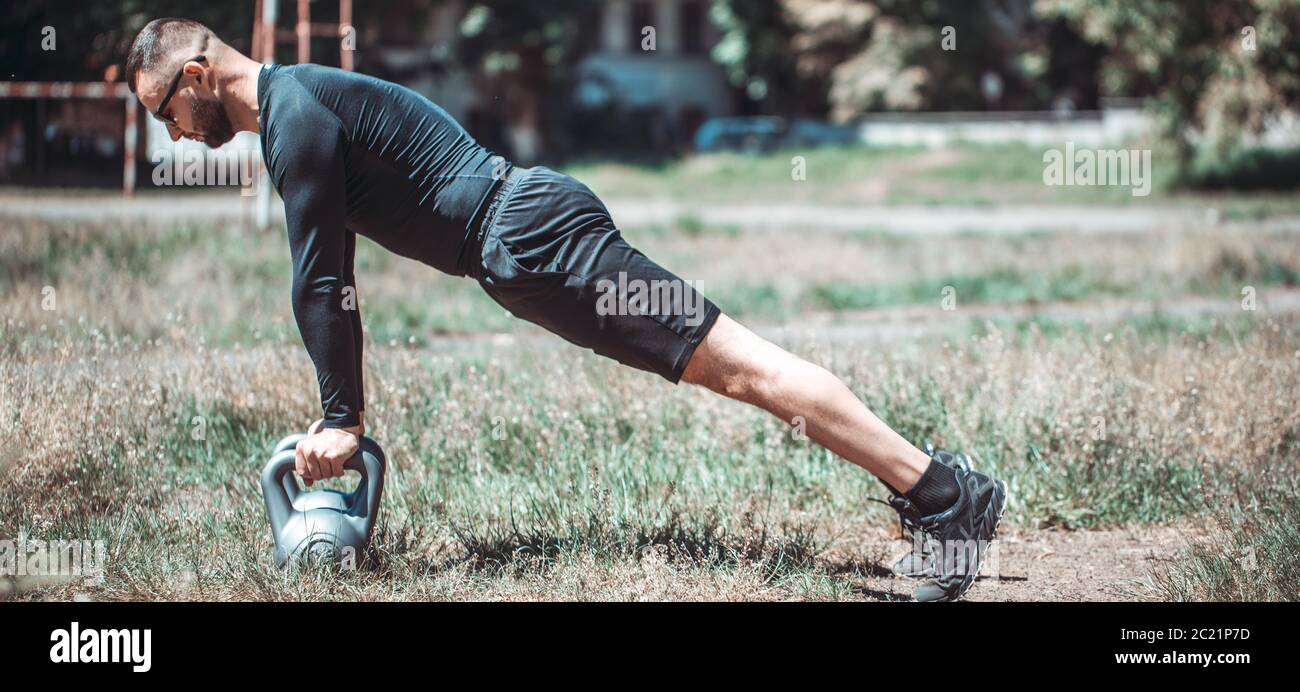 Athletic man working out with a kettlebell at street gym yard. Strength ...