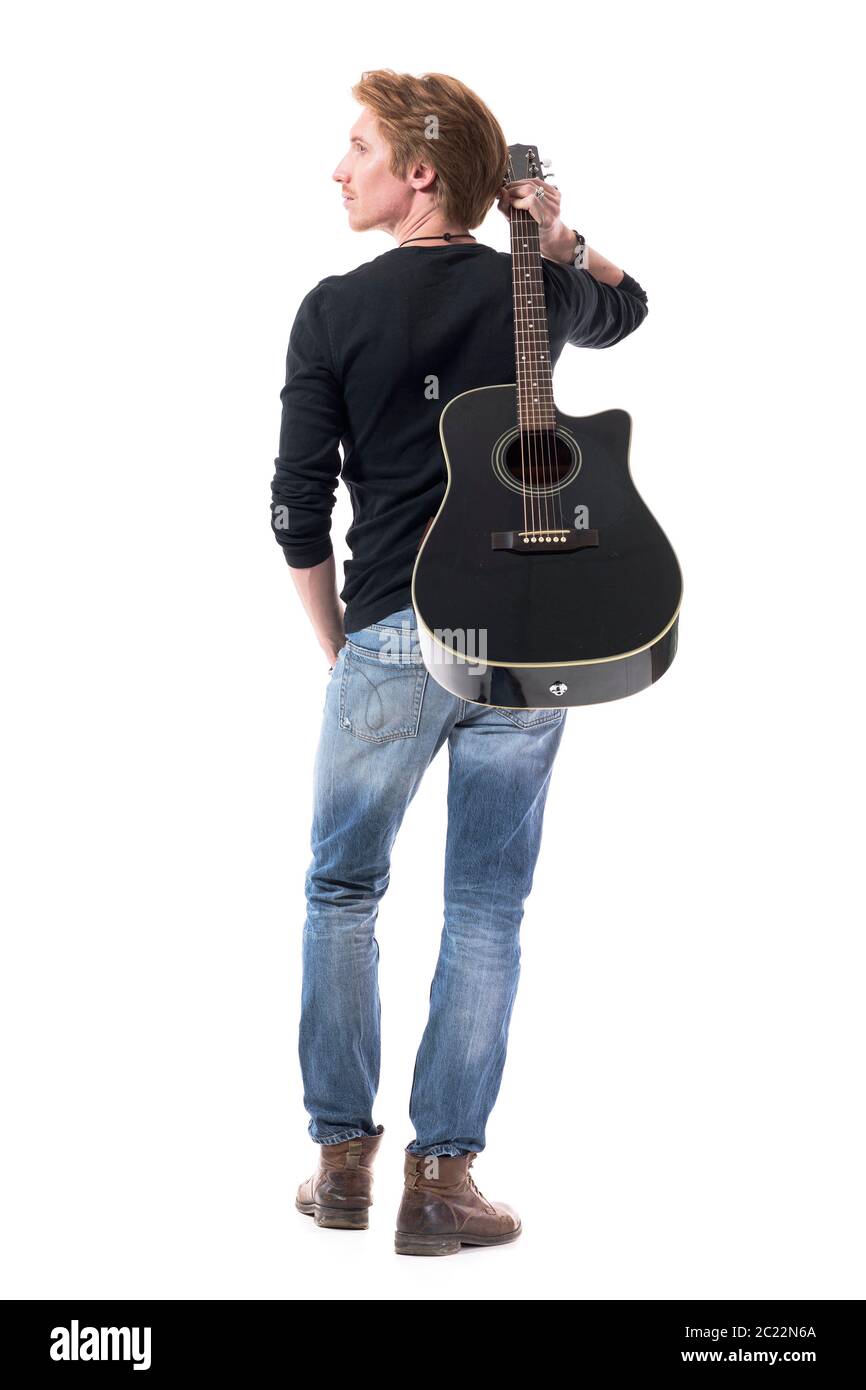 Back view of young rocker musician carrying guitar on shoulder looking ...