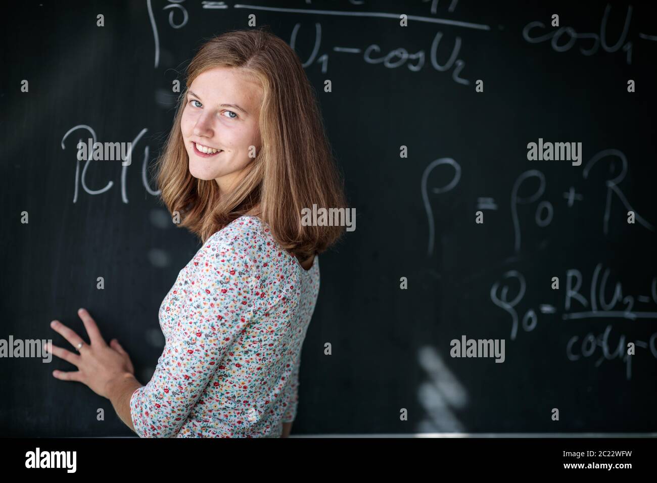 Pretty, young female student/teacher in front of a blackboard during ...