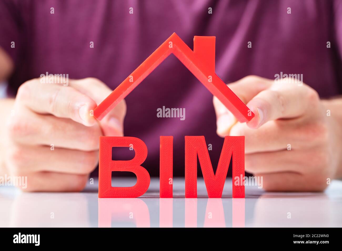 A Person's Hands Holding Roof Over BIM Text On Reflective Desk Stock ...