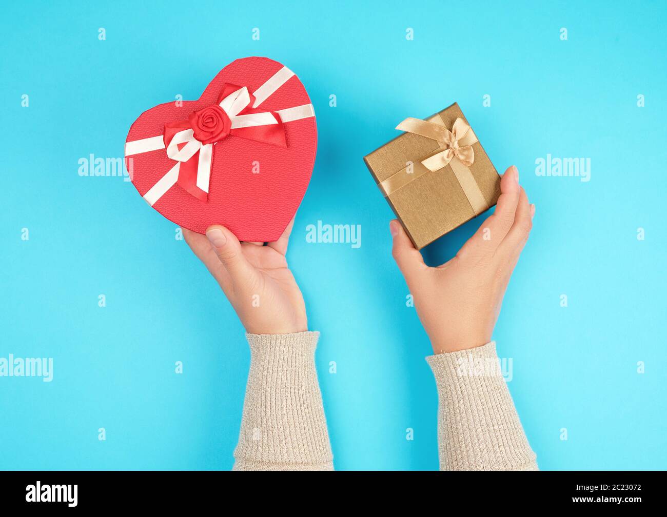 two hands hold a paper closed boxes on a pink background, festive ...