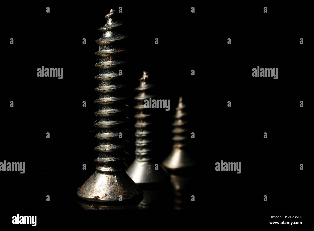 Three screws are placed on a reflective surface in a descending order ...