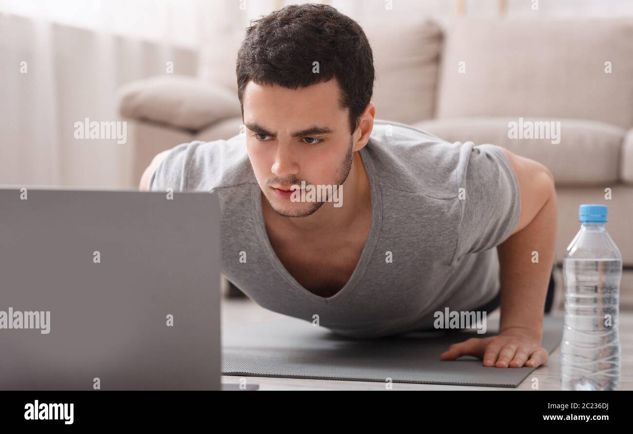 Modern home workout with online lessons. Young man does push ups on mat ...