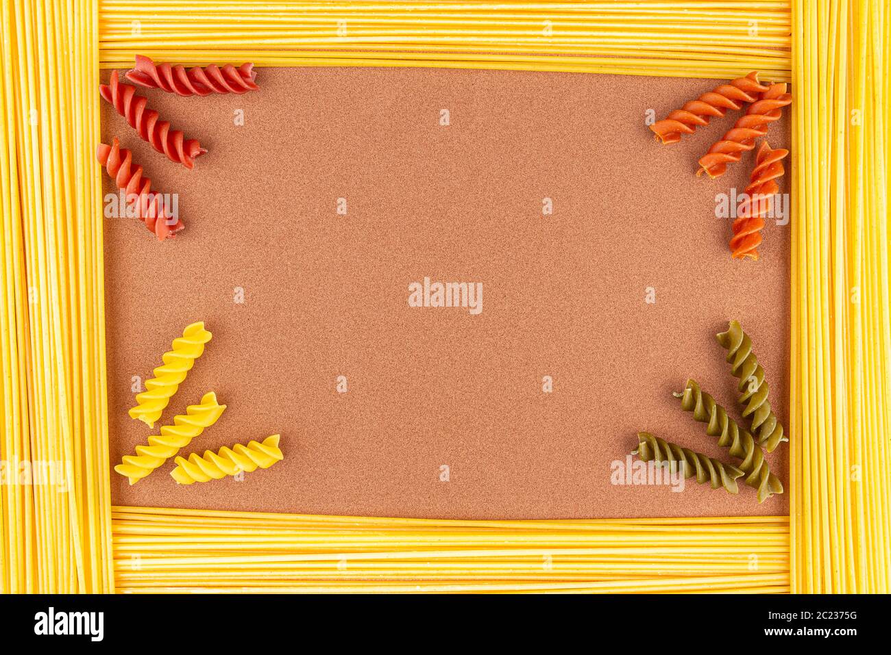 Frame made of spaghetti pasta on a brown foam background, colorful ...