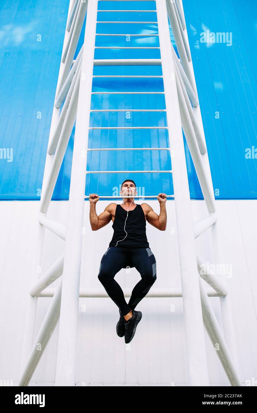Front view of attractive muscular guy is pulling-up, wearing black ...