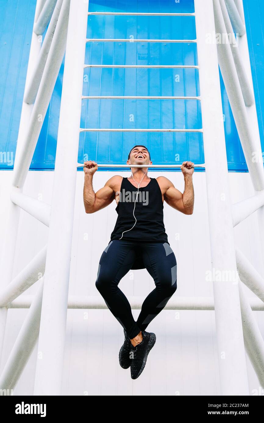 Front view of smiling handsome muscular guy doing pull ups, wearing ...