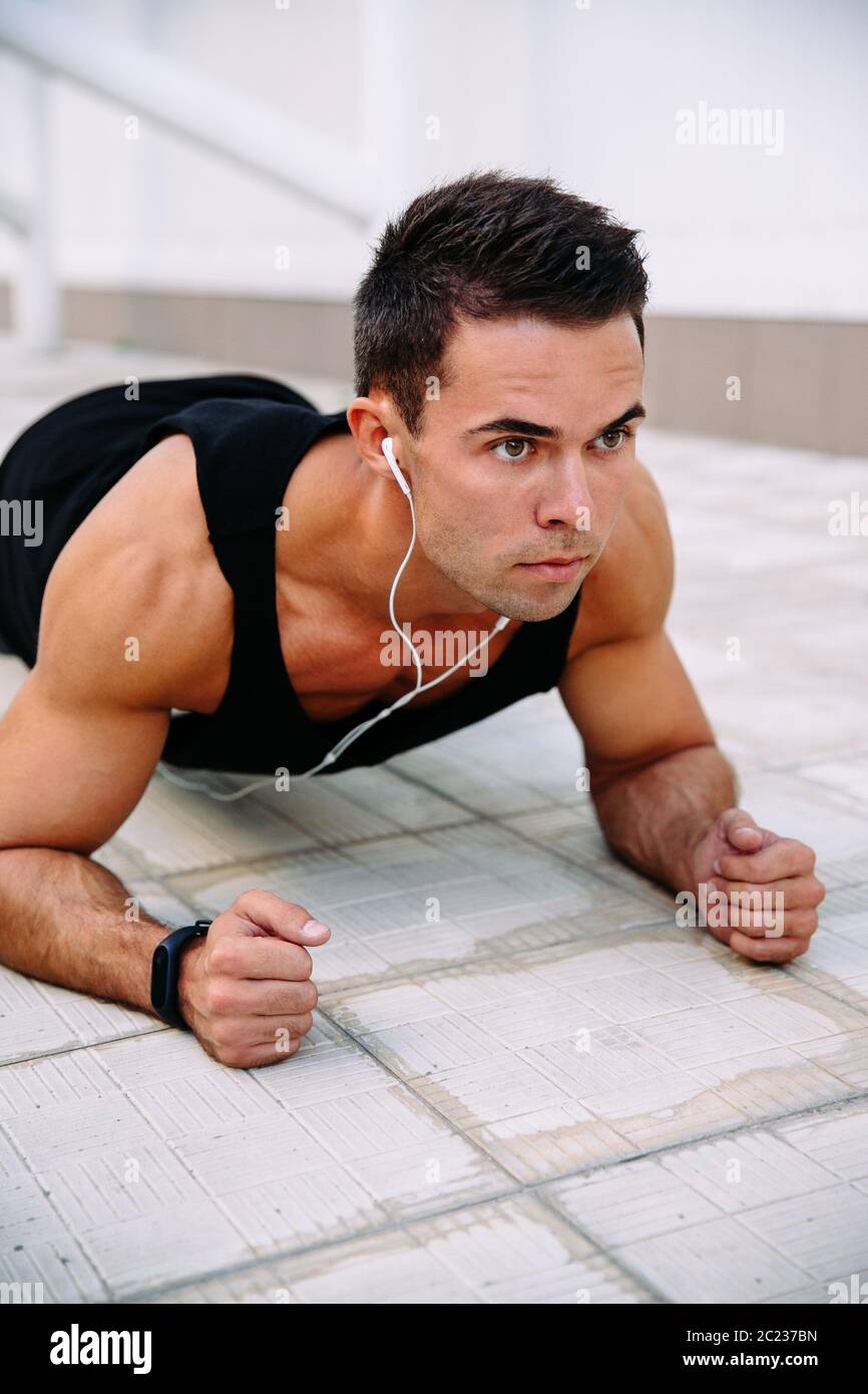 Close-up view of young muscular sportsman in earphones, doing push ups ...
