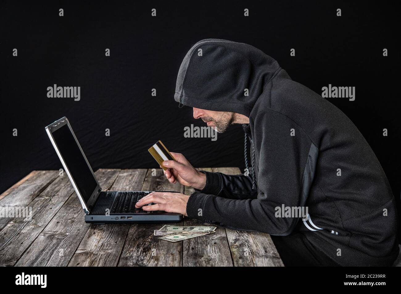 hacker in black hoody with laptop bank card and dollar notes in front ...