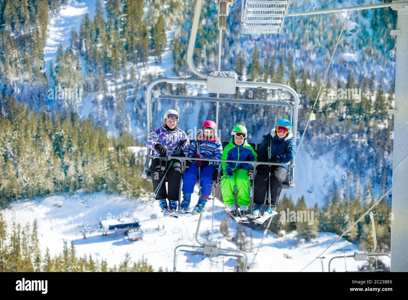 Four friends kids sit high together on chairlift lifting on the ...