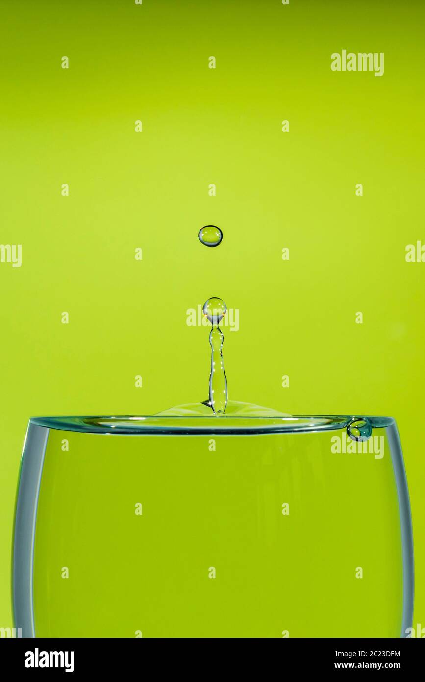 Indoor studio image of a high-speed falling water drop against a green ...