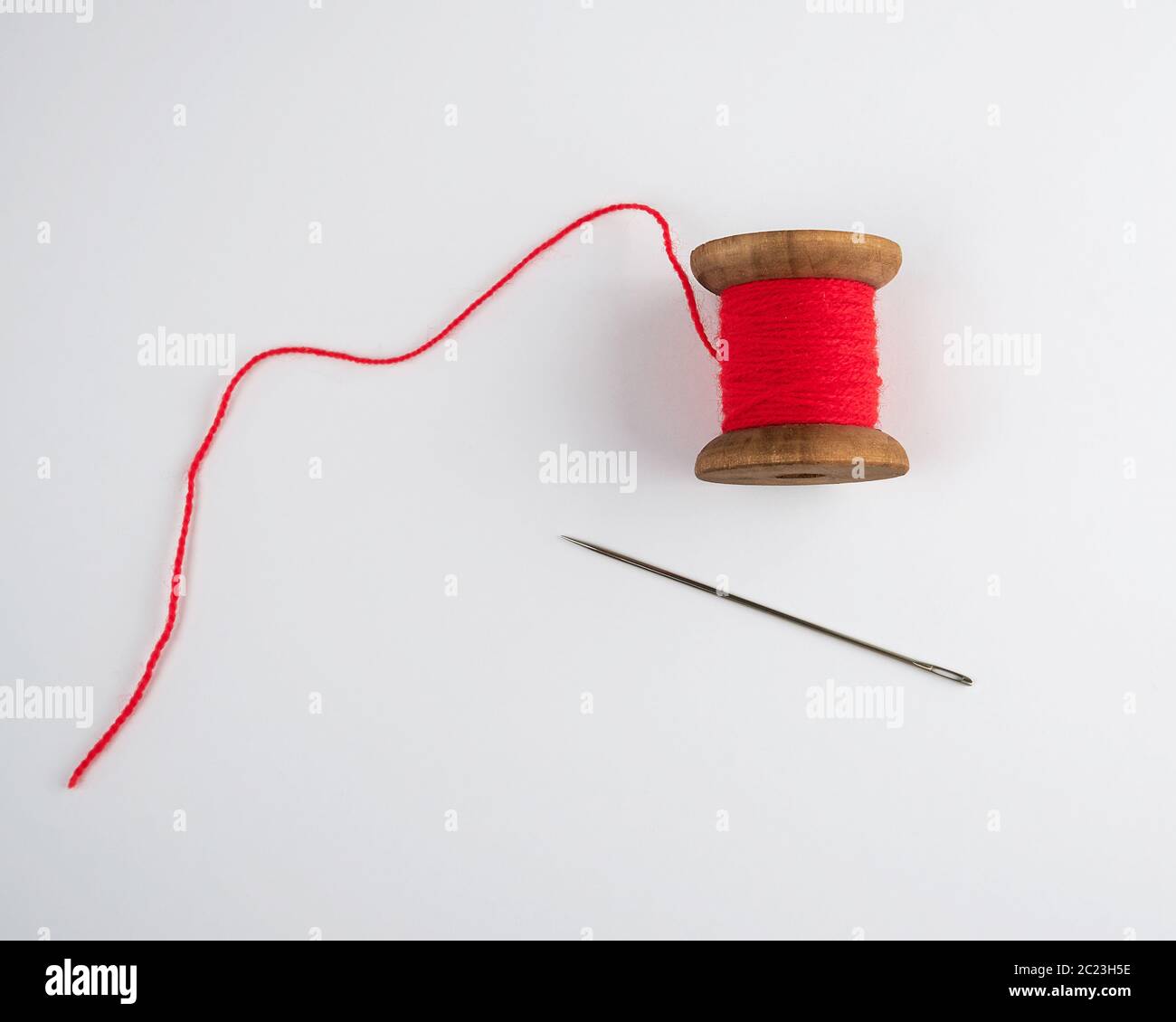 wooden reel with red wool thread and a large needle, white background ...