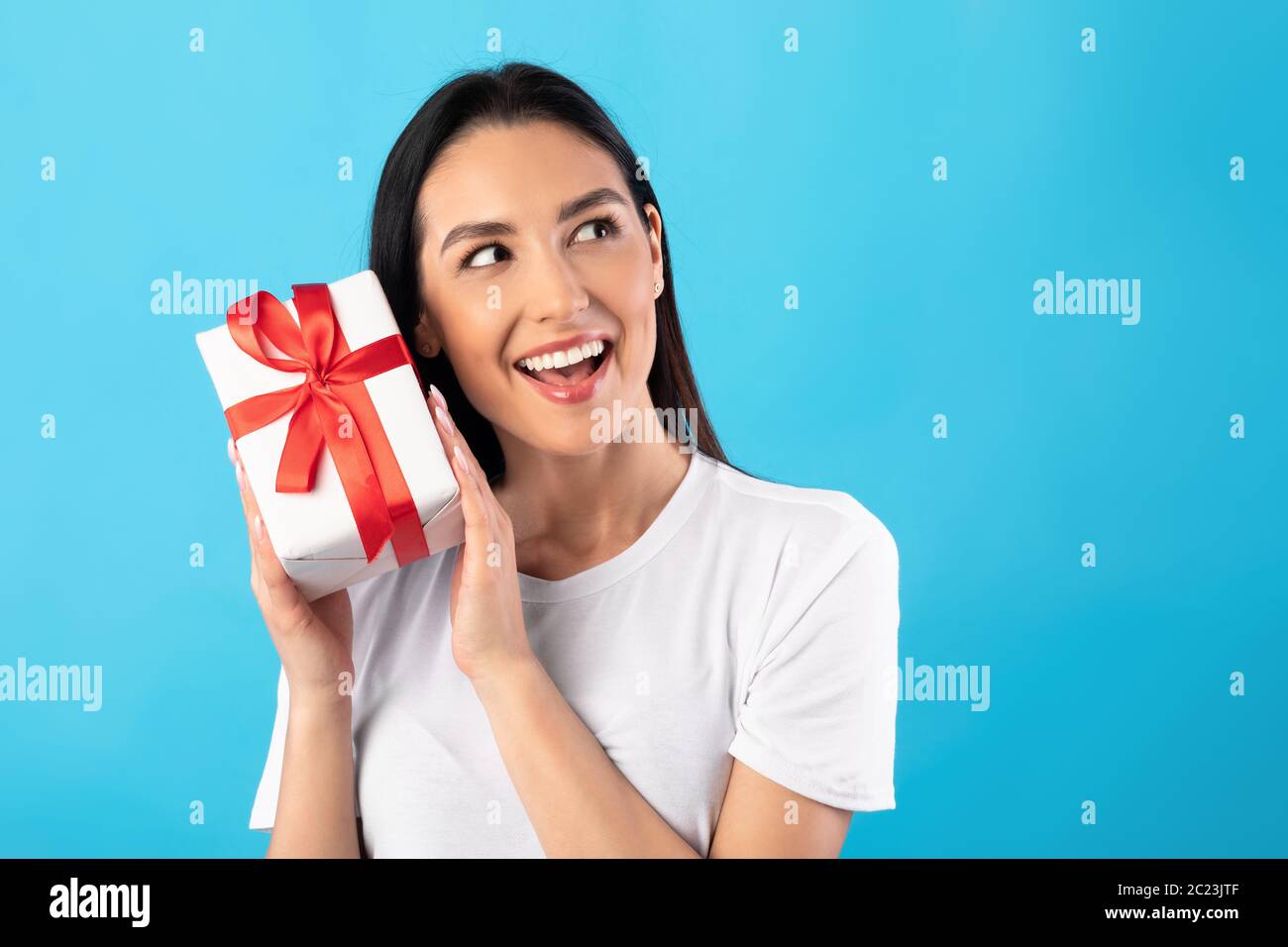 Happy girl shaking gift box at turquoise studio Stock Photo - Alamy