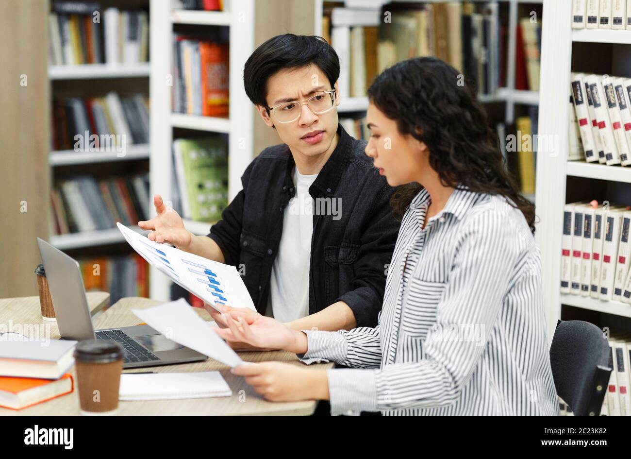 Two students discussing charts and diagrams in library Stock Photo - Alamy