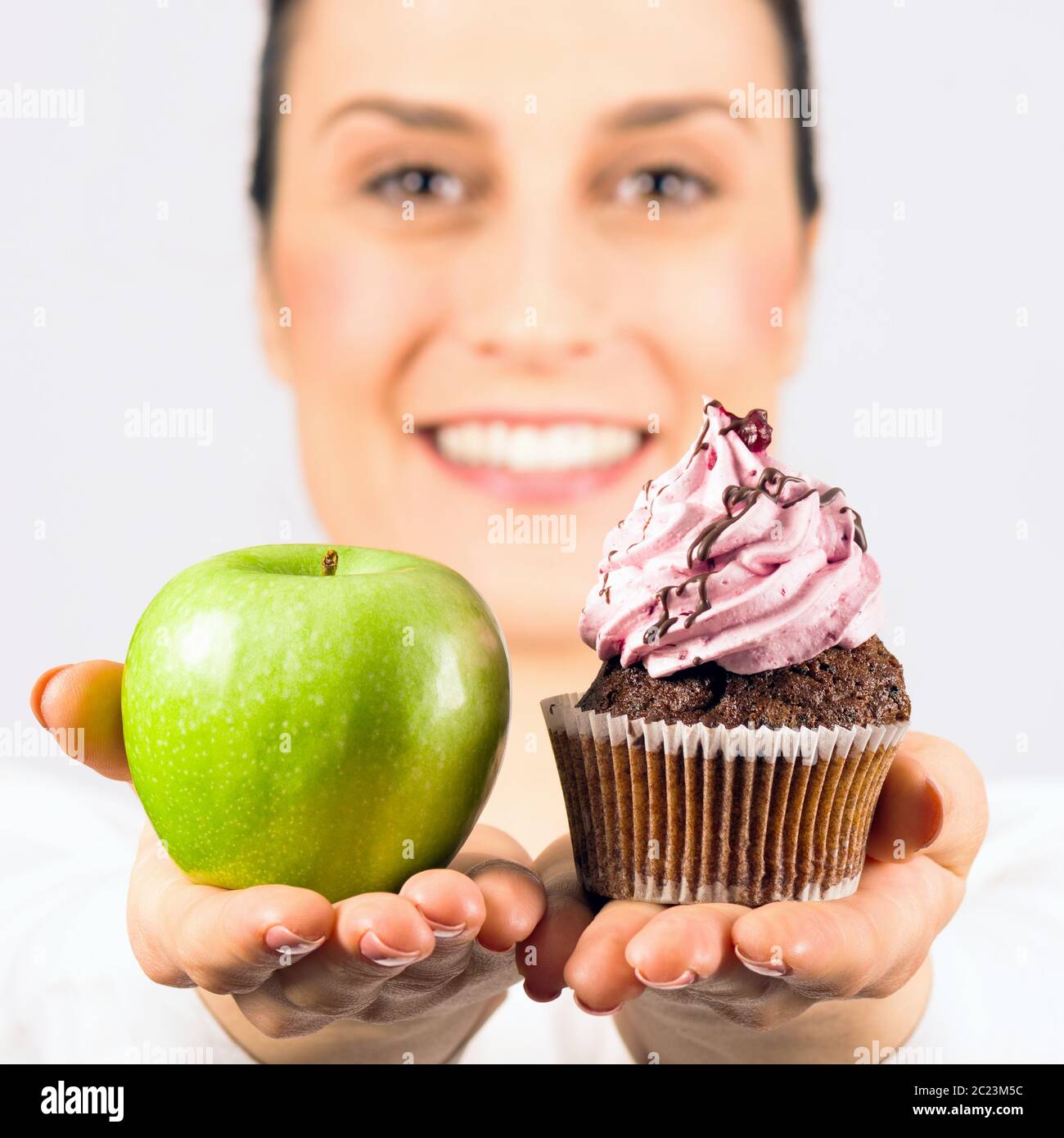 Smiling woman gives a choice, deciding apple or cupcake, healthy or ...