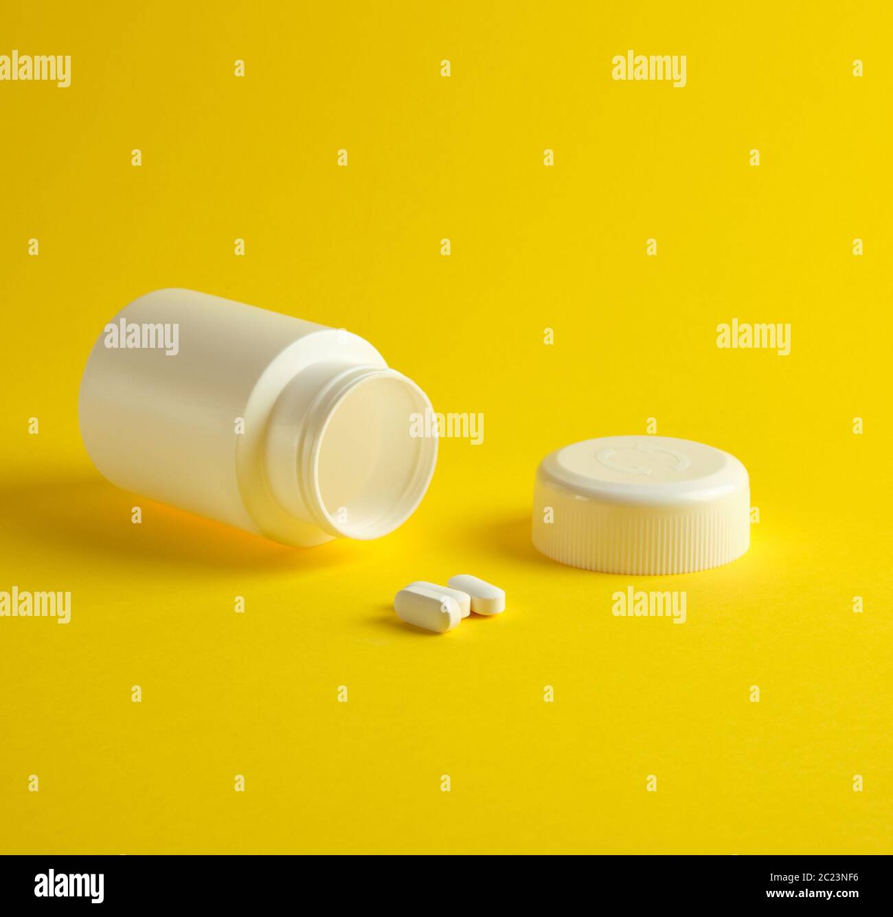 open white plastic jar for medicines and oval pills on a yellow ...