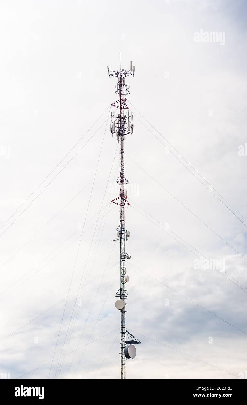 Tall red and white metal communications antenna tower with dishes and supporting cables, against ...