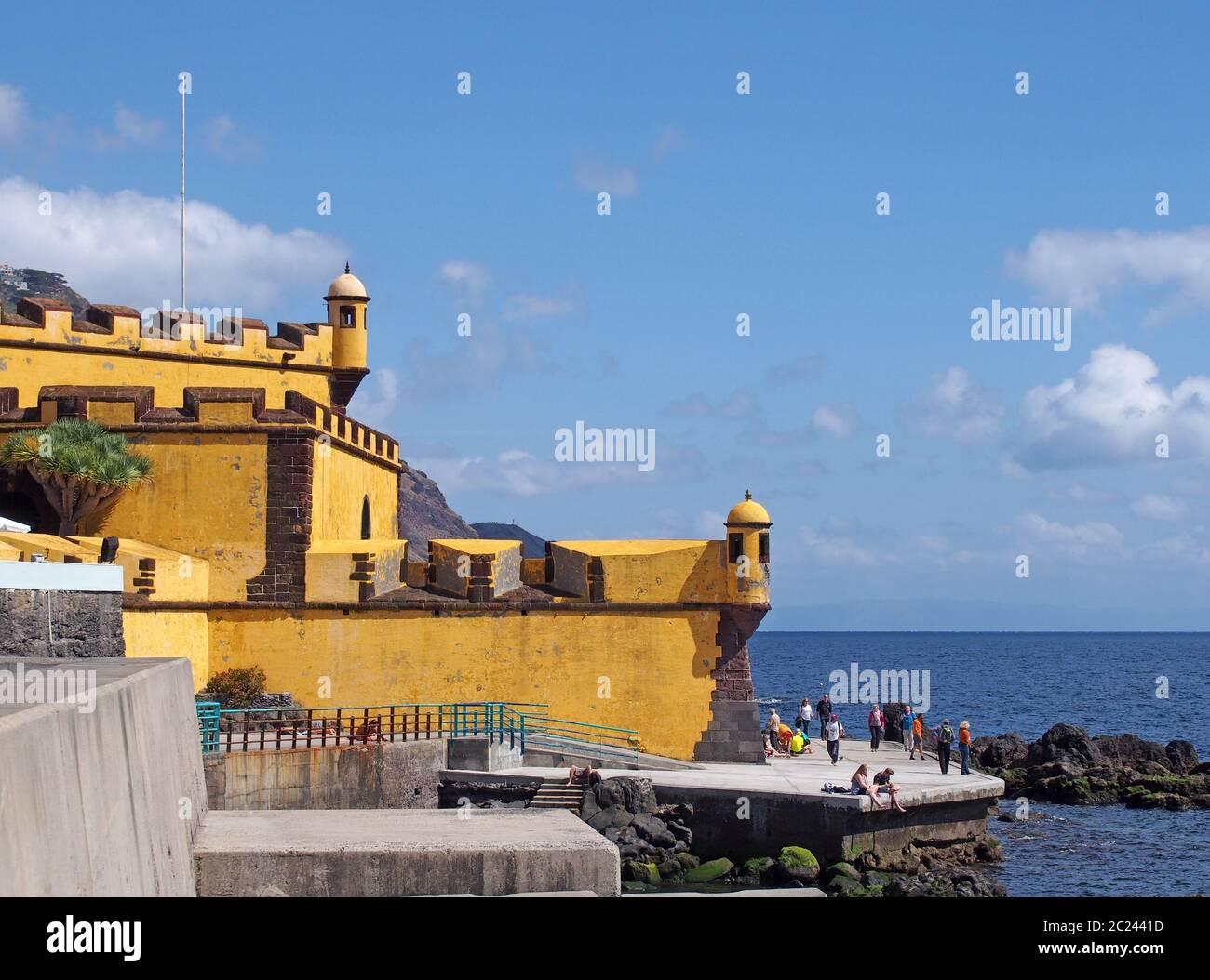 tourists relax by the sea outside the yellow fort in funchal madeira in ...