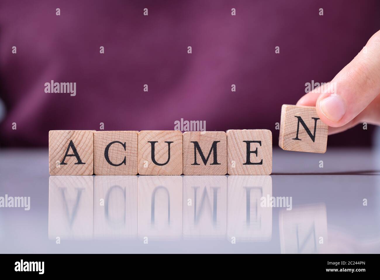 A Person's Hand Placing Last Alphabet Of Word Acumen Over White ...