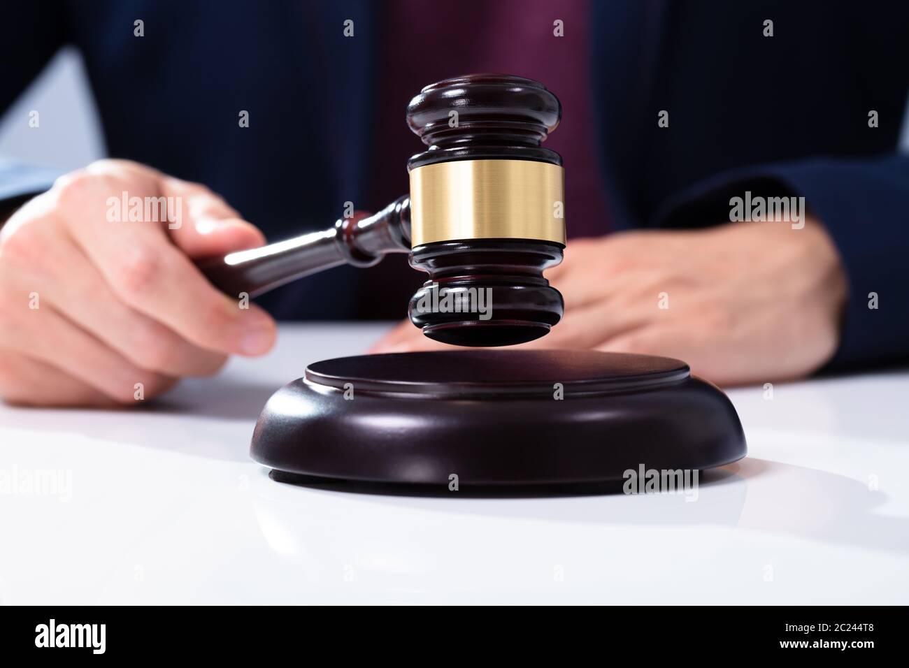 Judge's Hand Striking The Gavel On Sounding Block Over White Desk In ...