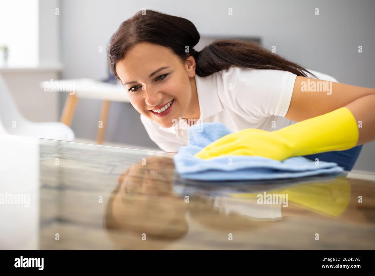 Side View Of Female Janitor Cleaning Desk With Blue Napkin In Office ...