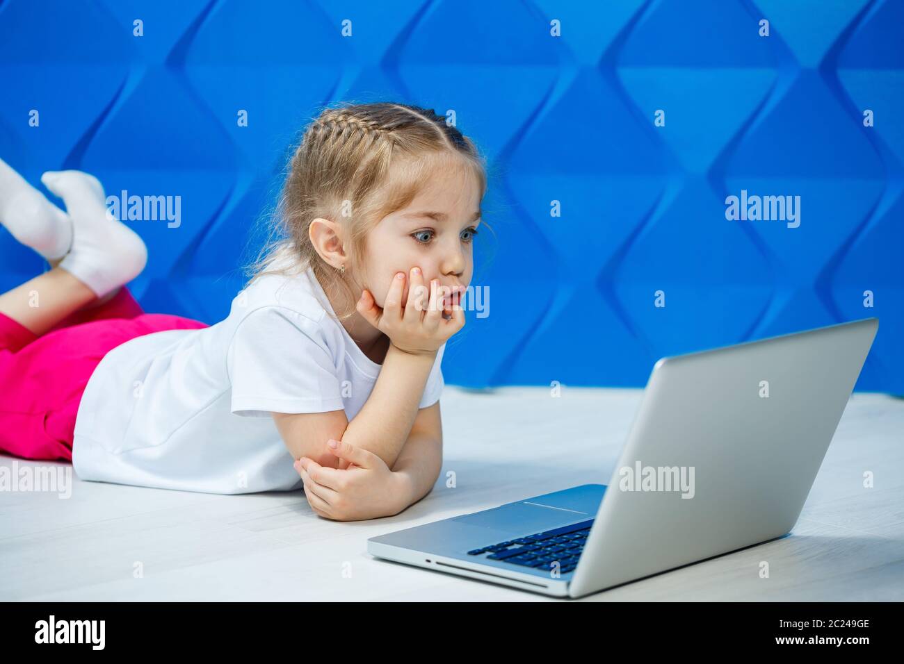 A modern child girl uses a laptop lying on the floor with legs looking ...