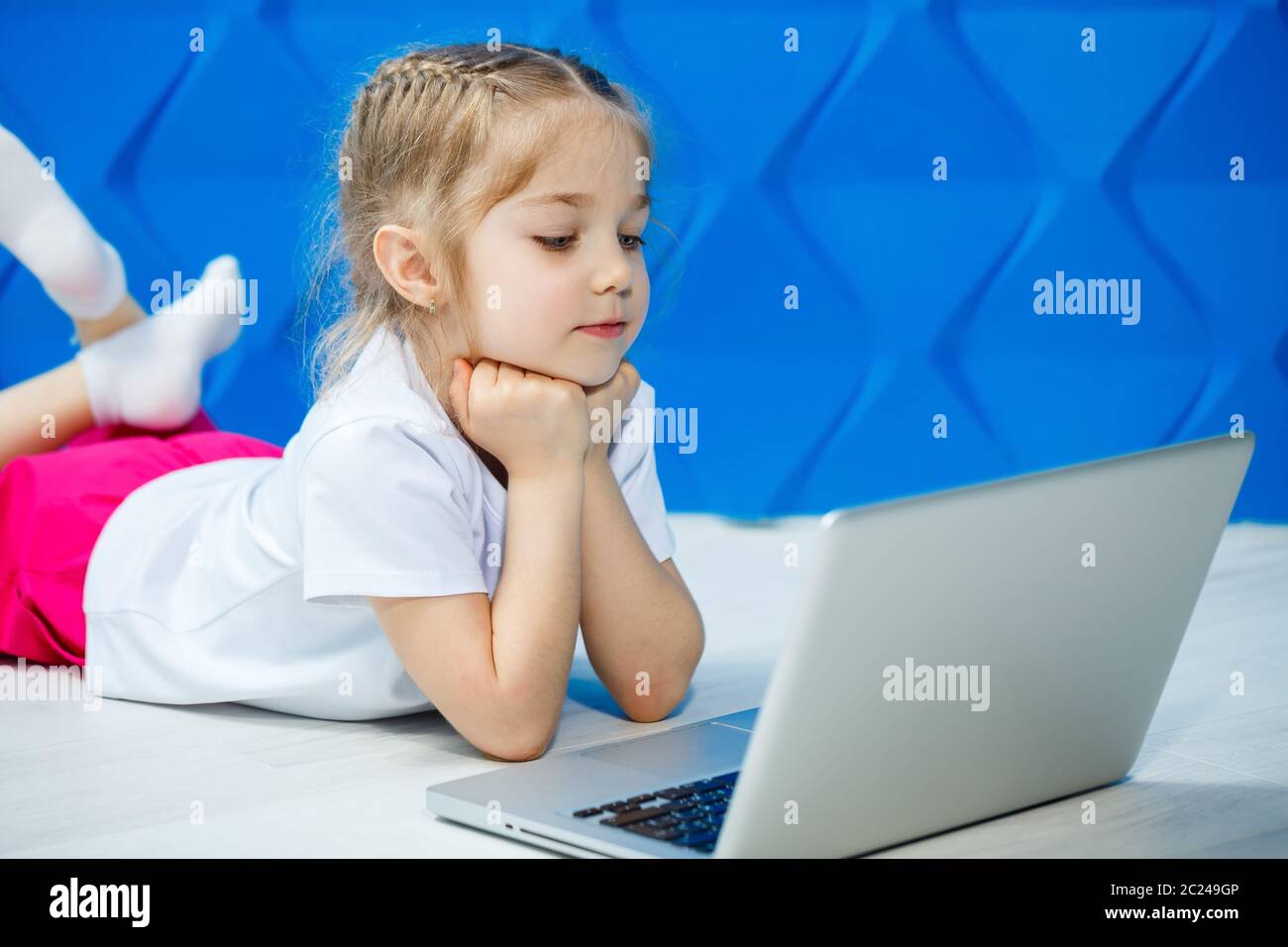 A modern child girl uses a laptop lying on the floor with legs looking ...