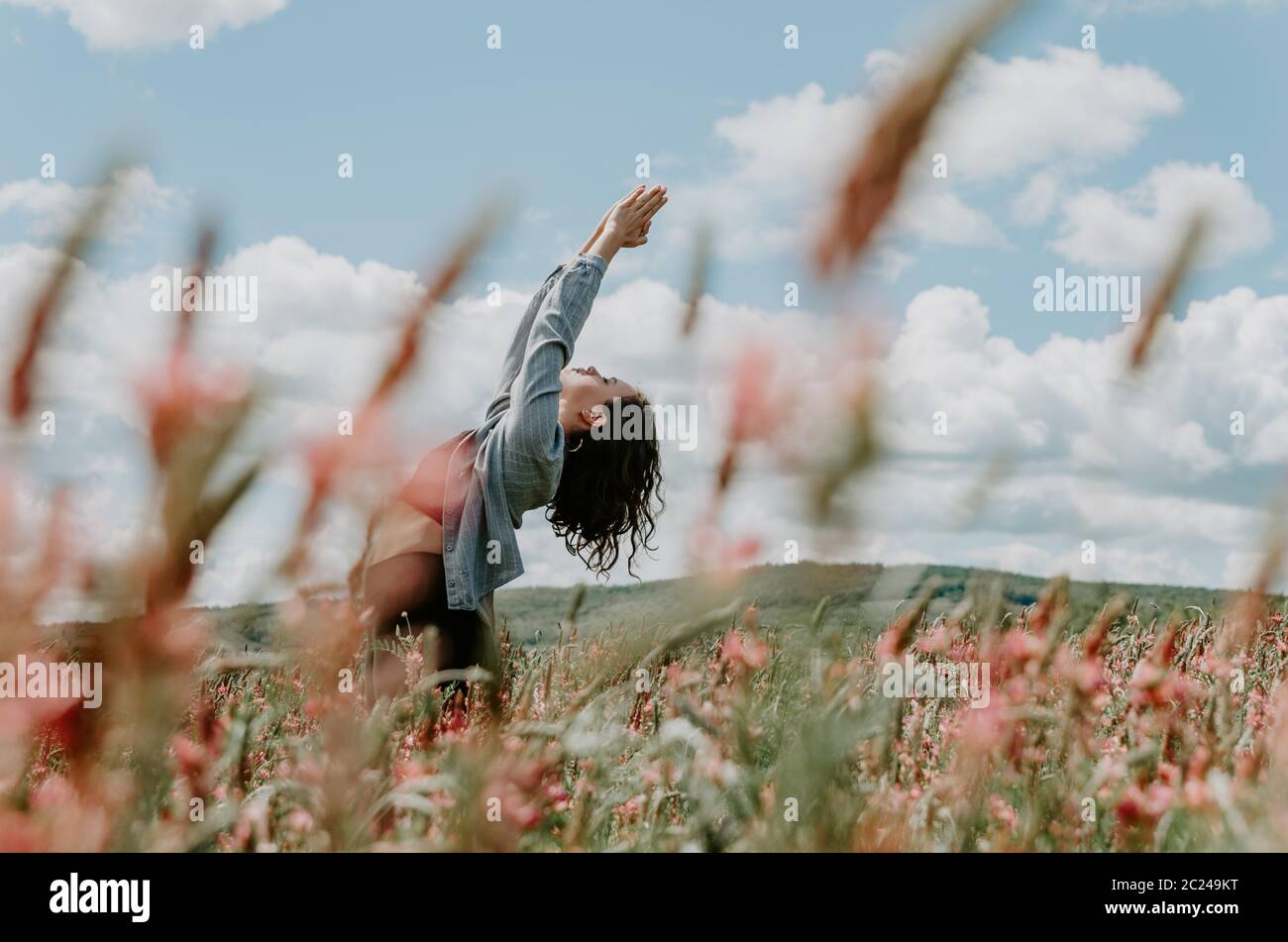 Young woman doing a standing back bend with arms up in flower field ...