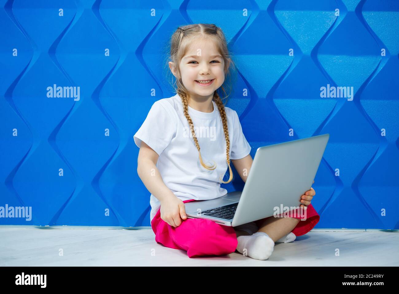 A modern child girl uses a laptop lying on the floor with legs looking ...