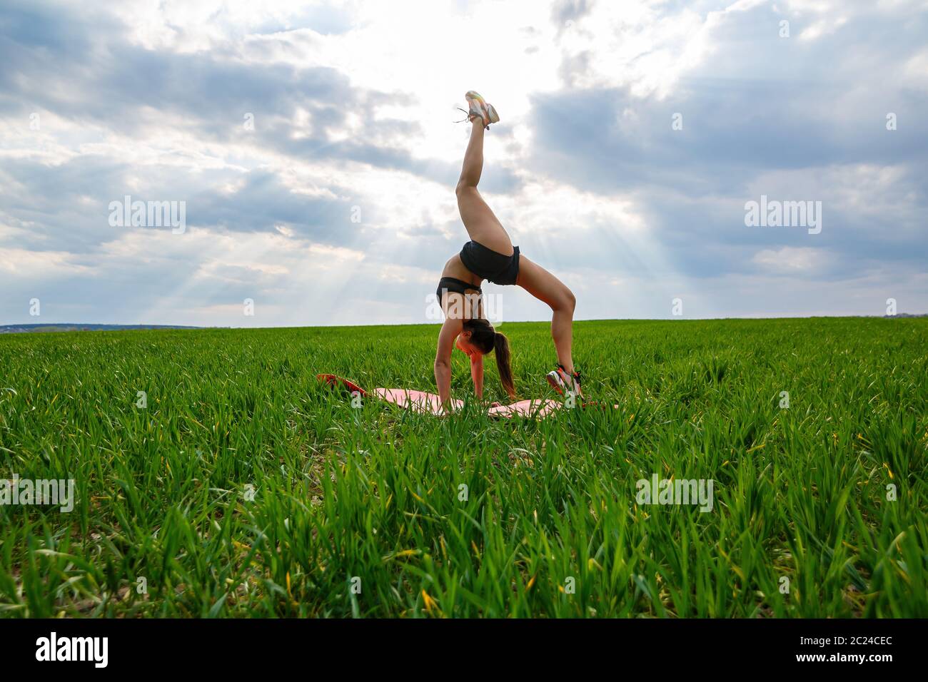 A young woman in a black top and shorts performs a handstand. A model ...