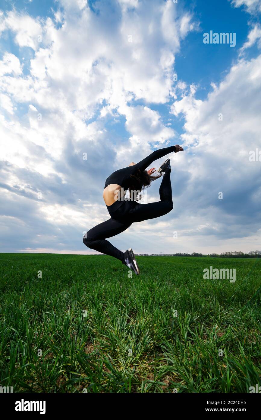 Young professional gymnast is jumping in nature against the blue sky ...