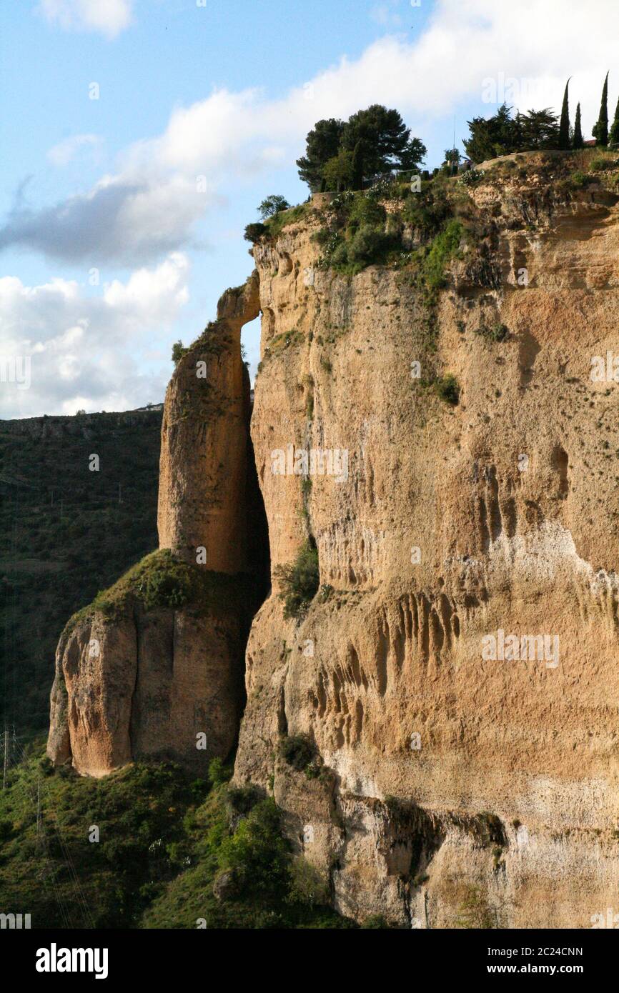 High rock wall with small connection by natural bridge to rock pillar ...