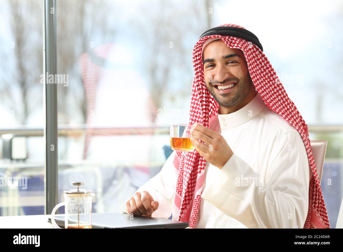 Happy arab man holding a cup of tea looking at camera sitting in a ...