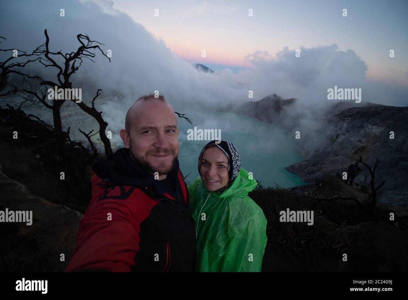 Couple travelers standing on edge of crater Ijen volcano with colorful ...