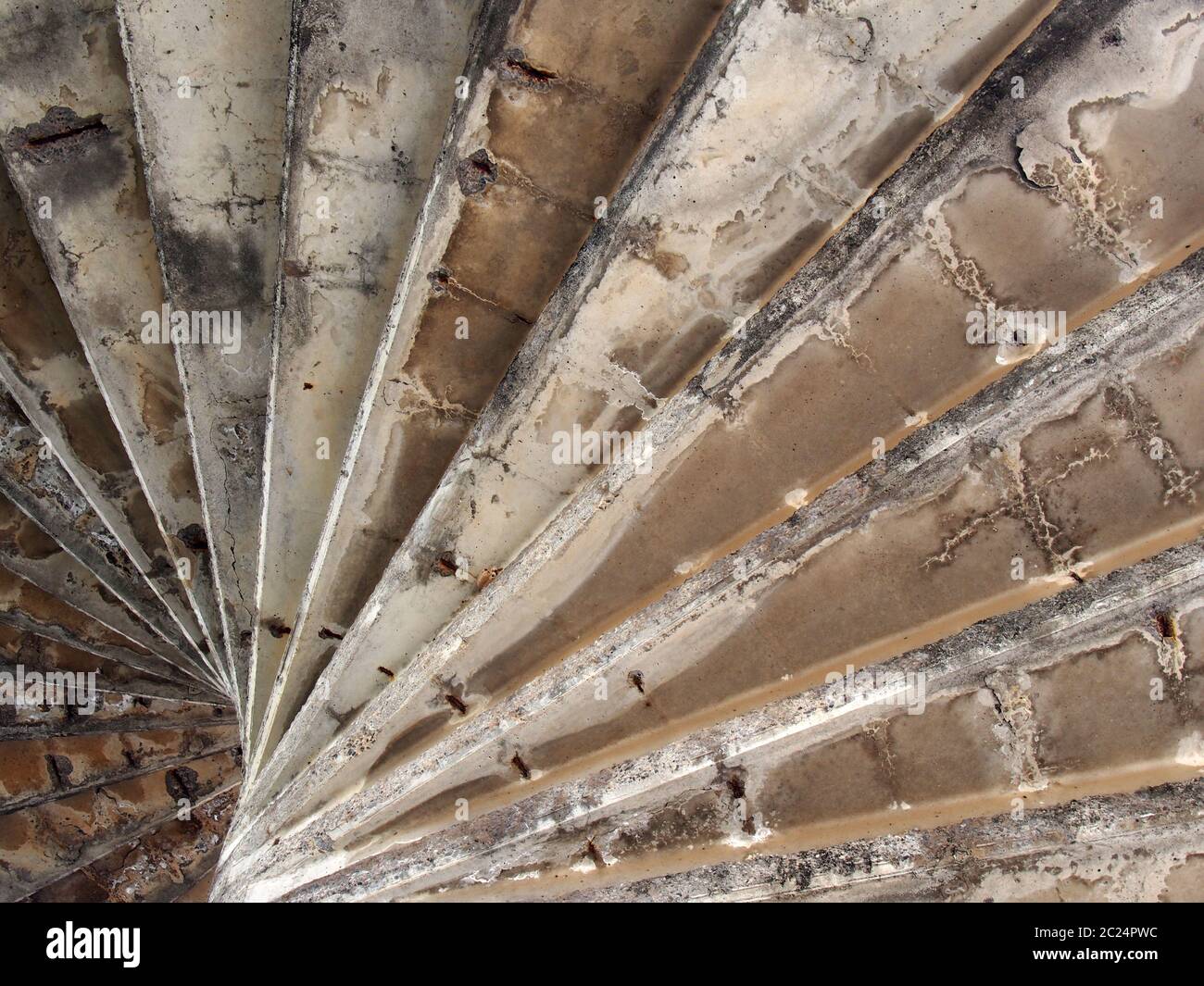 a view underneath old eroded brown worn concrete spiral stairs forming ...