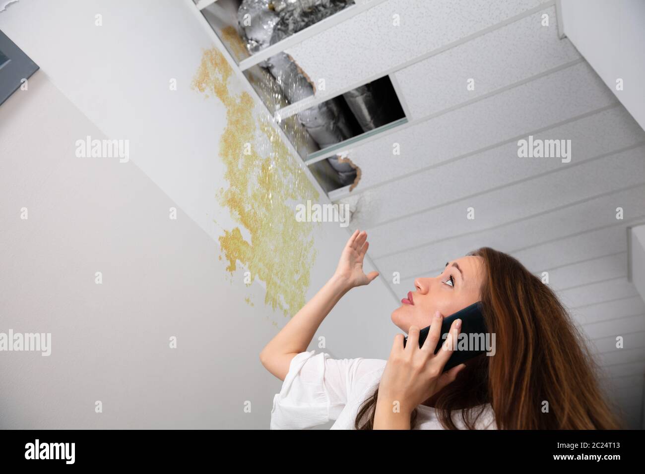 Sad Woman Calling Plumber While Looking At Leak Ceiling In Corridor ...