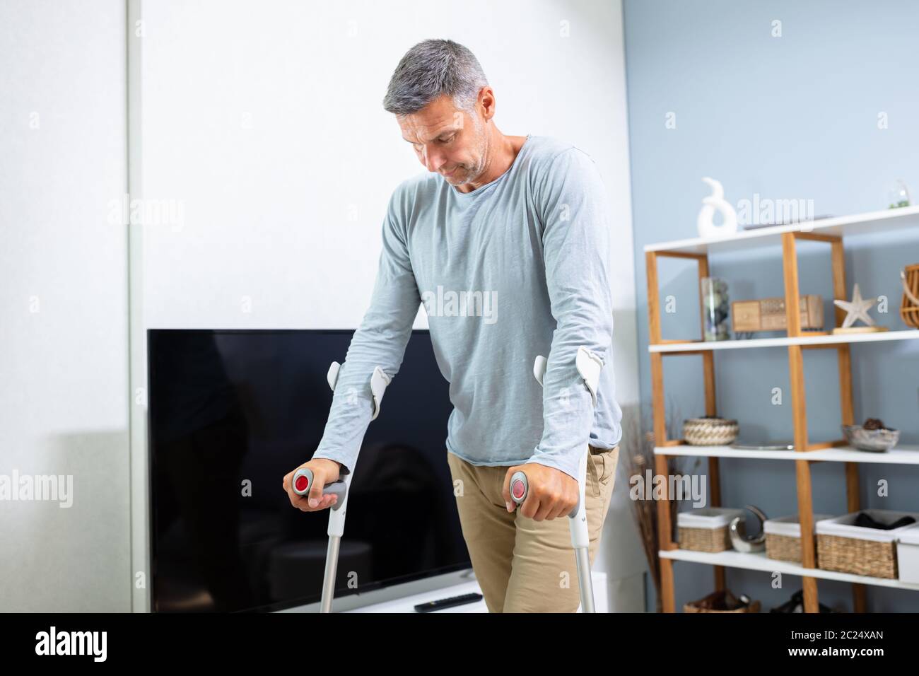 Disabled Man Using Crutches To Walk At Home Stock Photo - Alamy