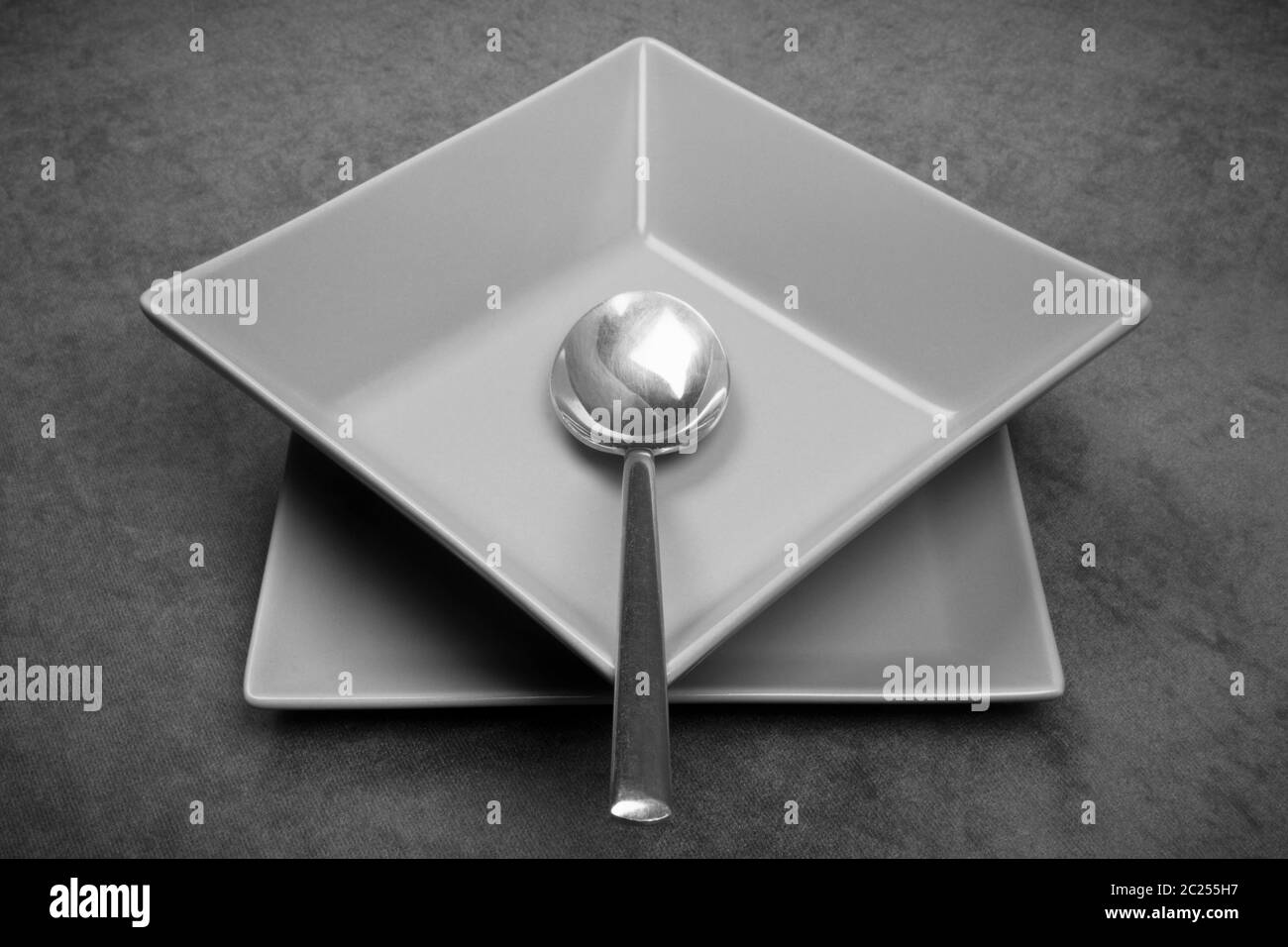 Gray square shape crockery, plates with spoon are on gray background ...