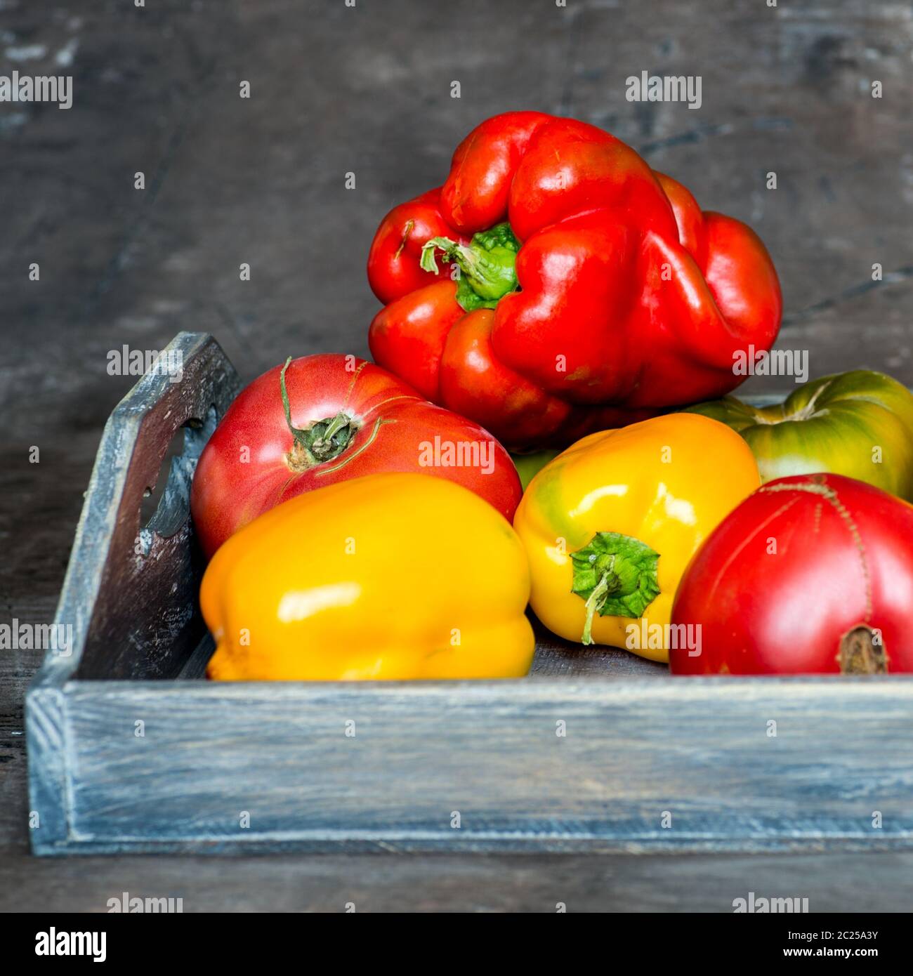 Imperfect natural peppers and tomatoes on an old wooden tray on a dark ...