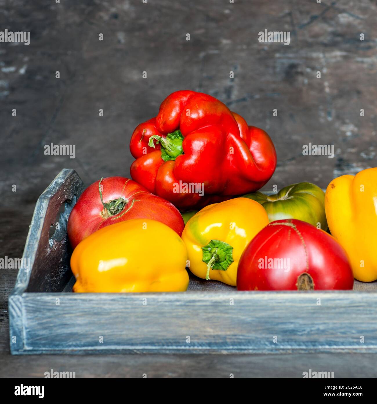 Imperfect natural peppers and tomatoes on an old wooden tray on a dark ...