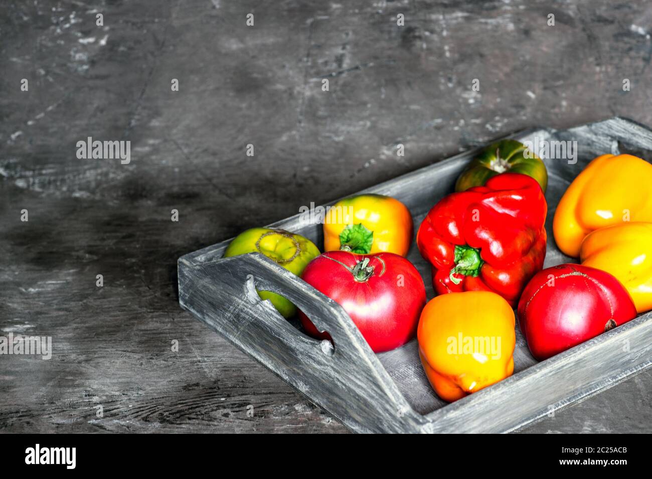 Imperfect natural peppers and tomatoes on an old wooden tray on a dark ...