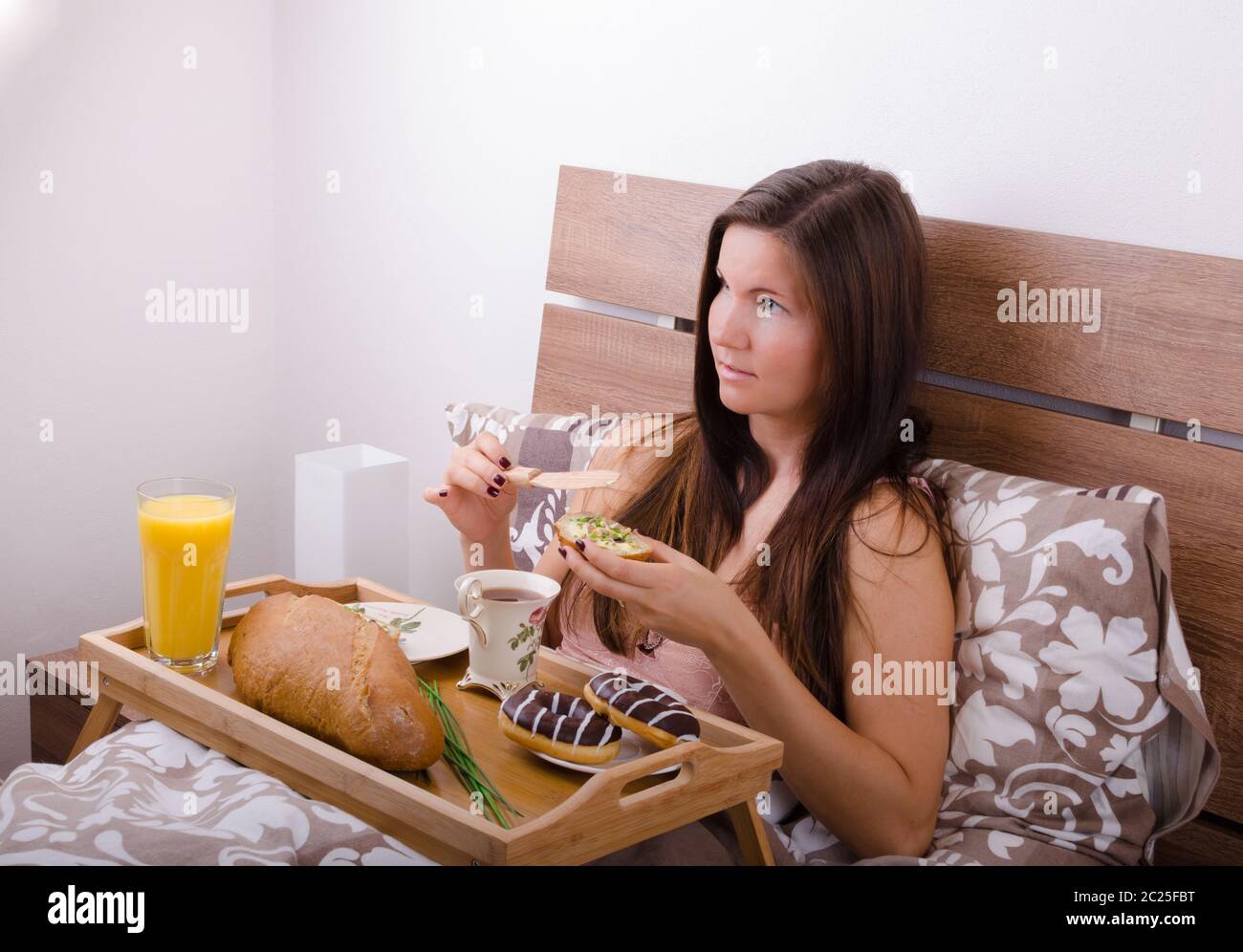 Beautiful young woman eating breakfast in bed in the morning, complete ...