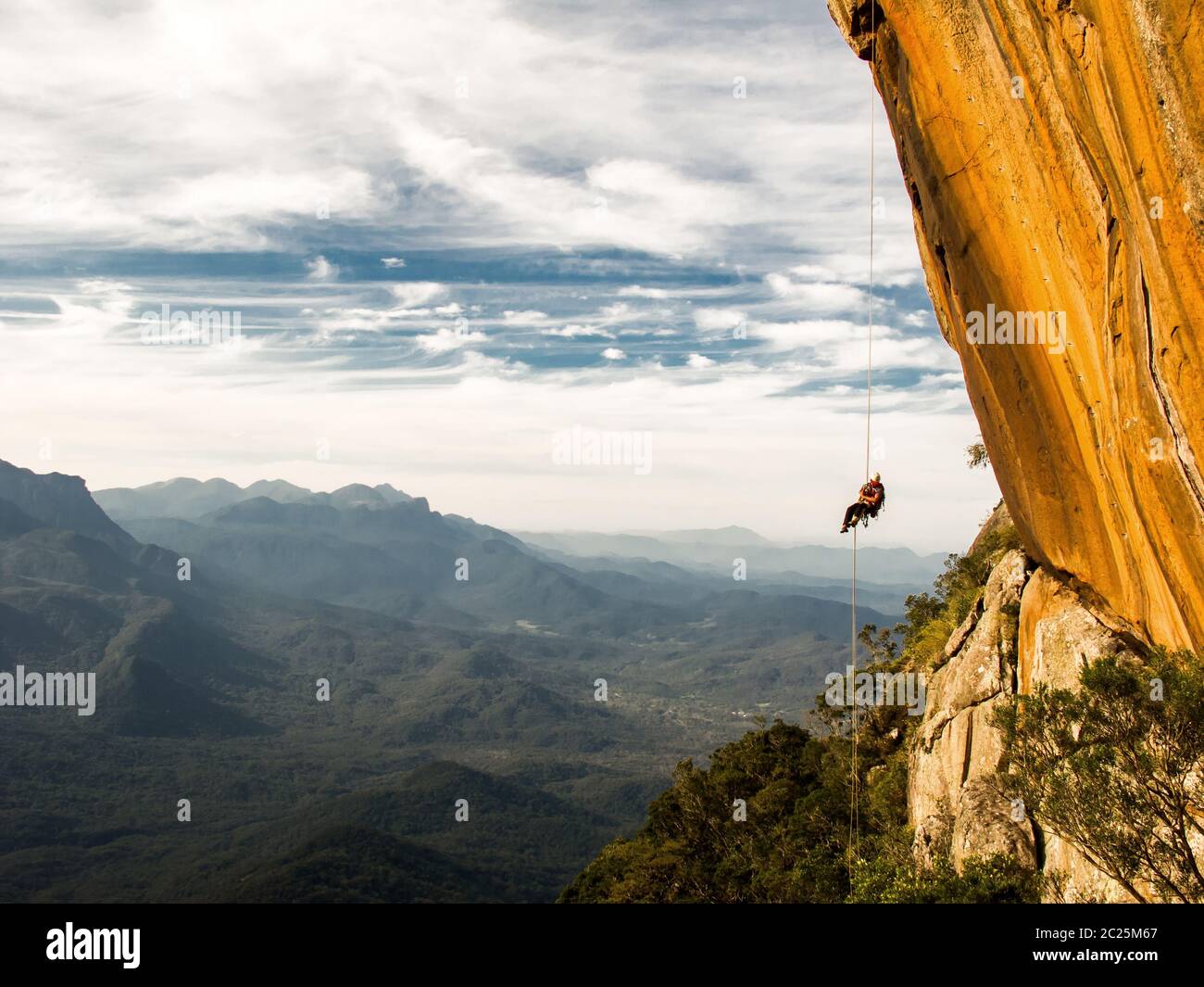 Abseiling a negative yellow rock wall with mountains on background ...