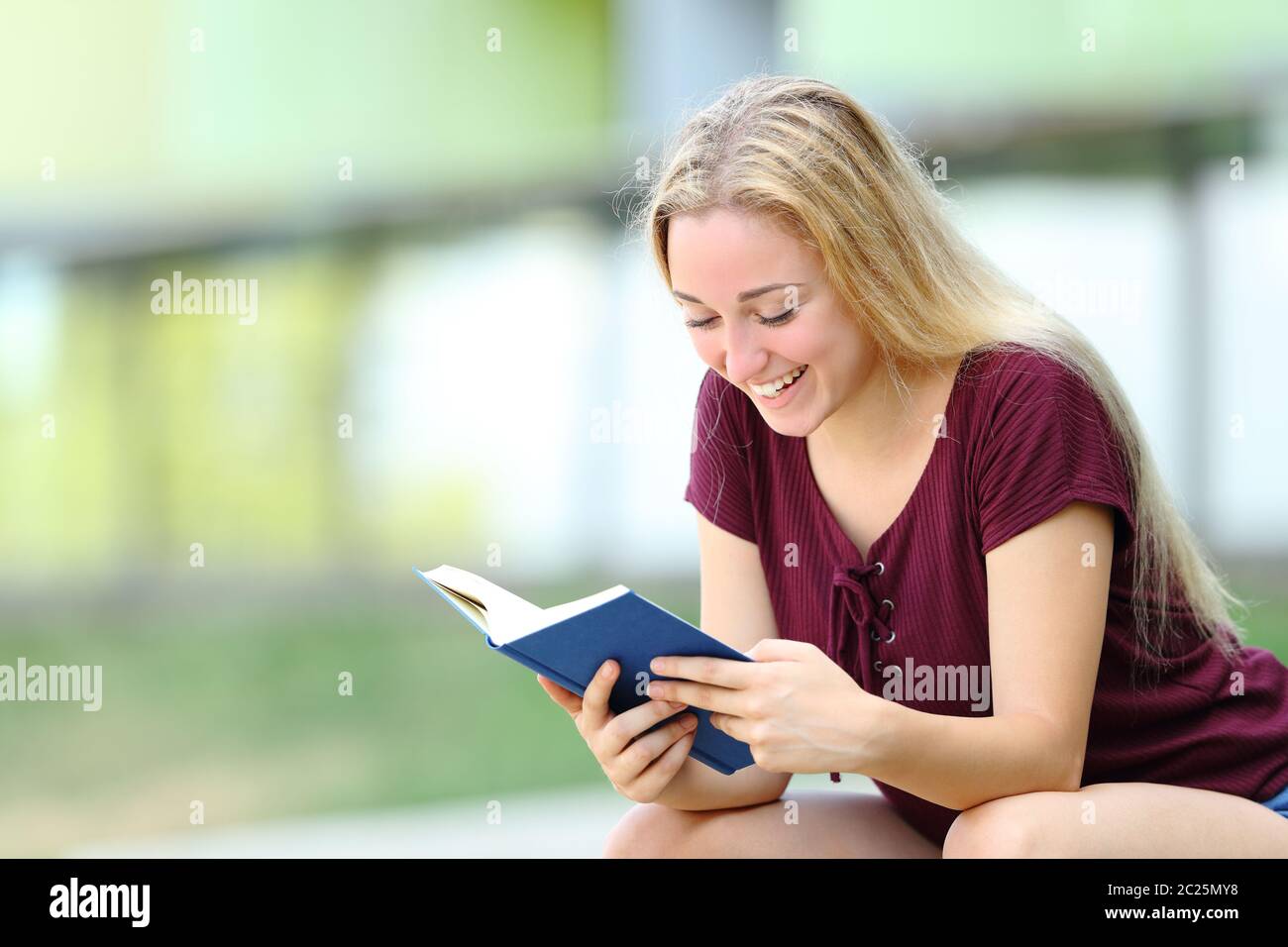 Happy student studying reading a paper book sitting outdoors in a ...