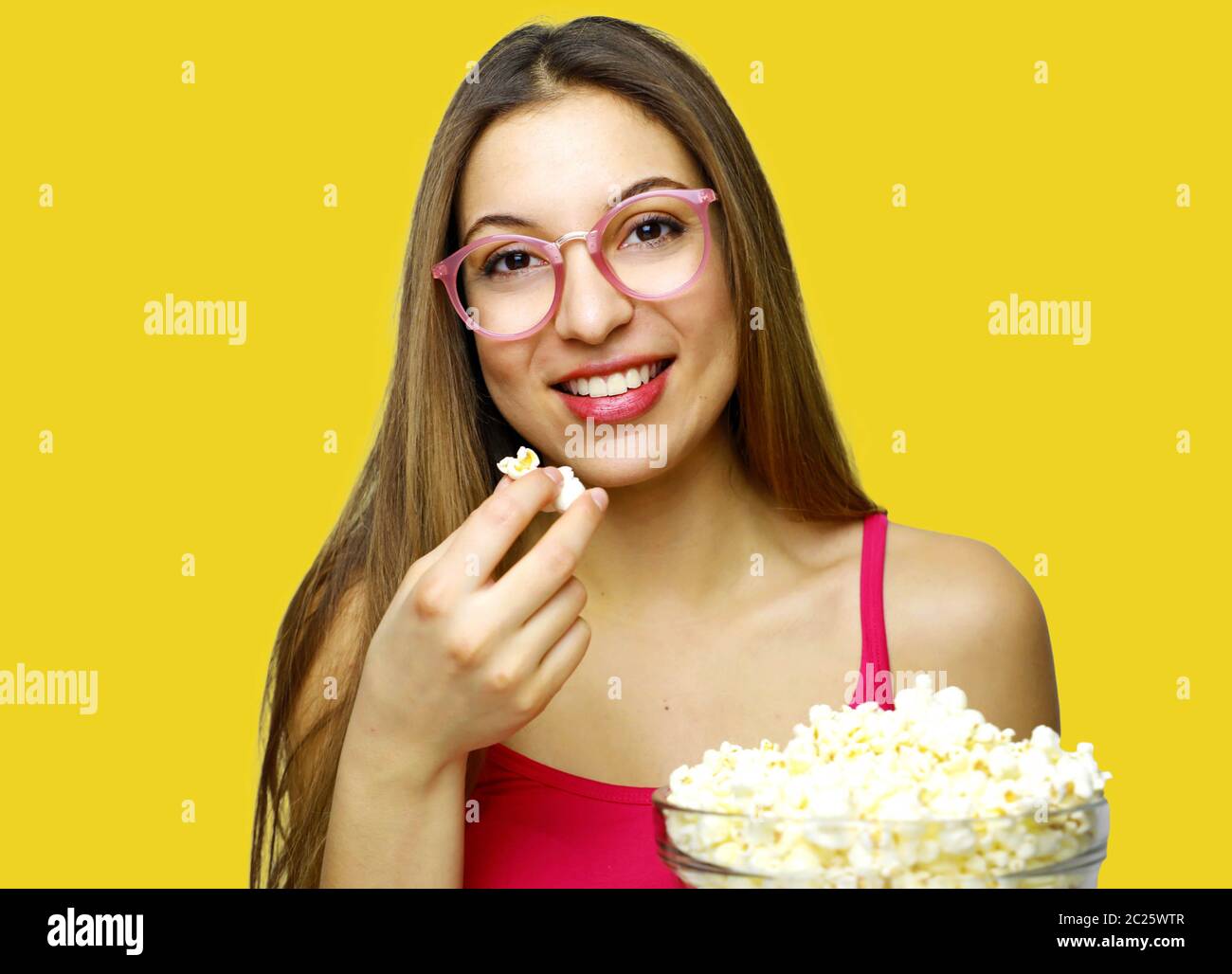 Portrait of cheerful young woman watching tv eating pop corn from bowl ...